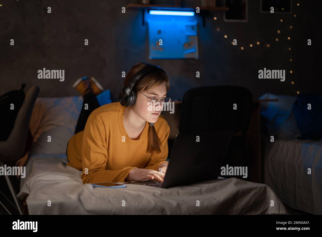 Female student studying at night on bed in dorm room using laptop ...