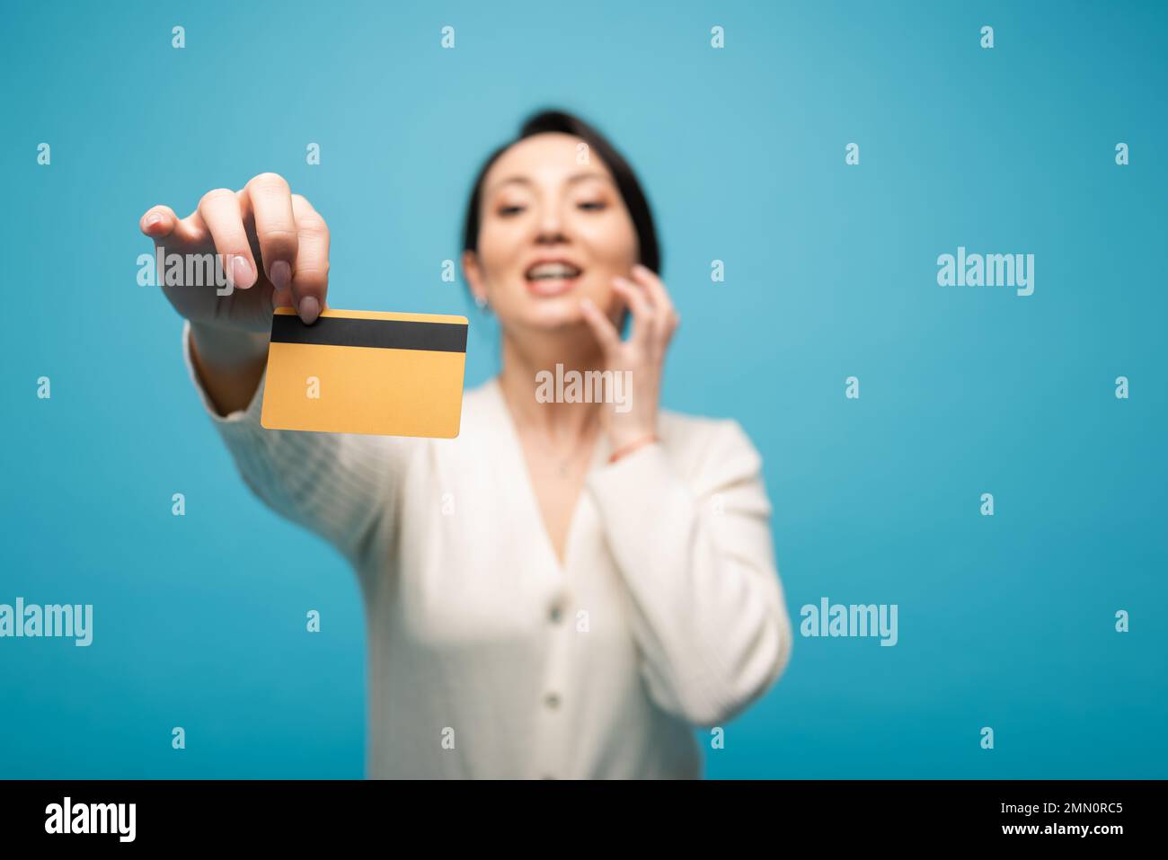 Blurred asian model showing credit card isolated on blue with copy ...