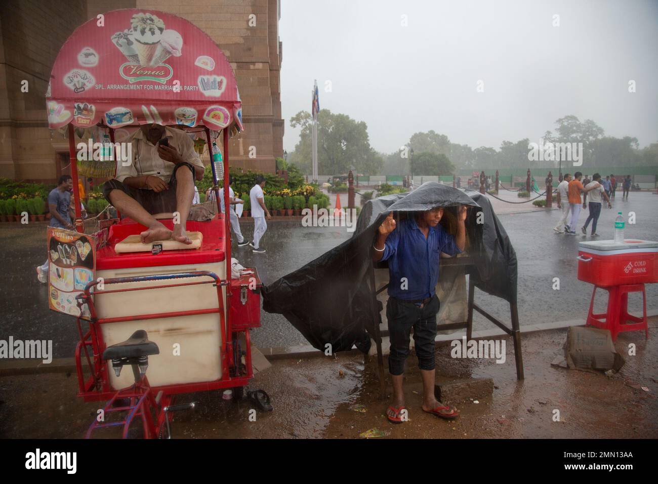 An Indian takes shelter under a plastic sheet as it rains at India Gate ...
