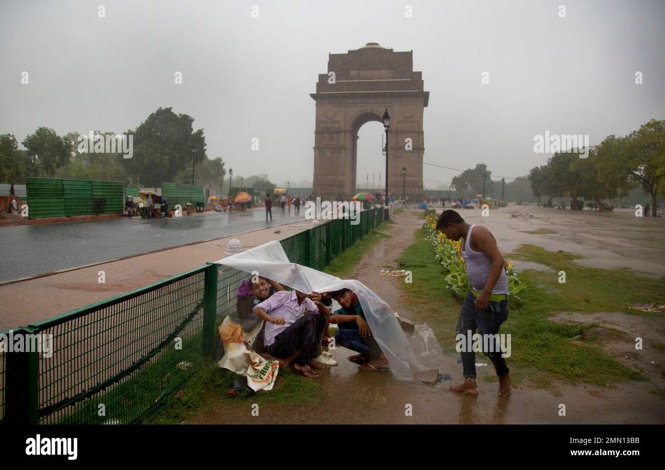 Indians take shelter under a plastic sheet as it rains at India Gate ...