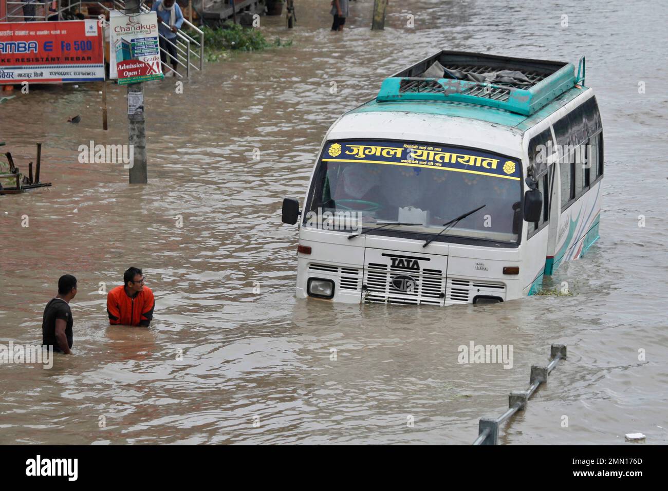 Nepalese men stand next to a partially submerged vehicle in Bhaktapur ...