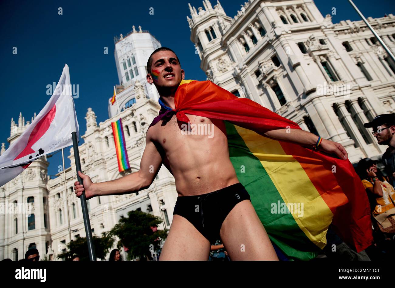 A participant wearing a rainbow colored flag walks past City Hall during the Gay Pride ...