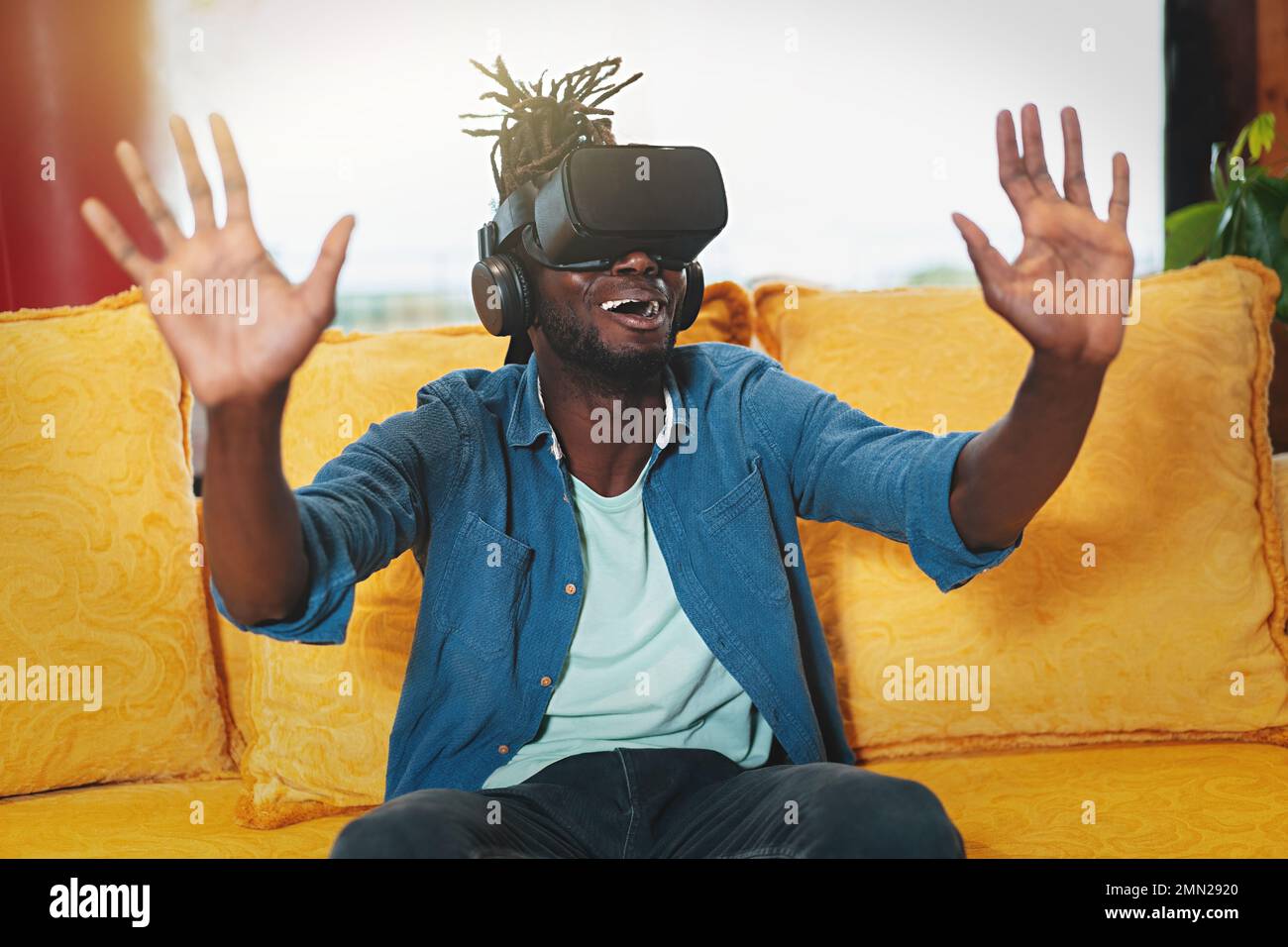Young African American man sitting on couch, enjoying VR experience and ...