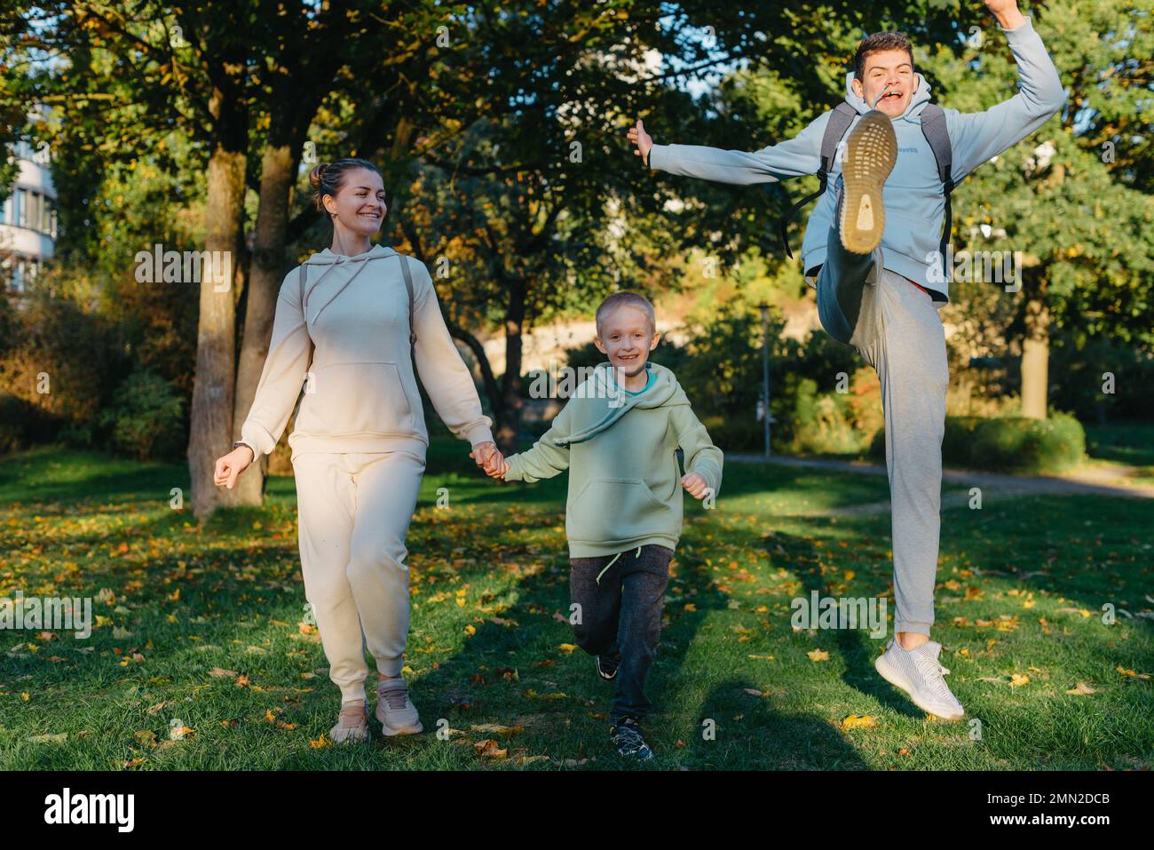 a family mom and 2 sons are having fun, running in the park and jumping ...
