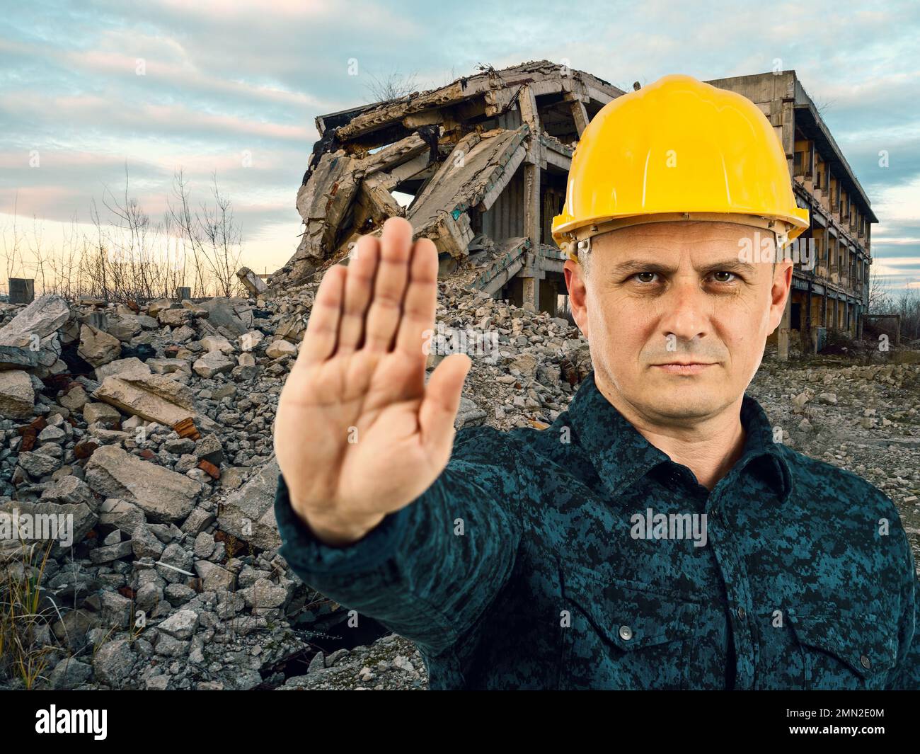 Engineer in hard hat making stop sign in front of ruined buildings ...