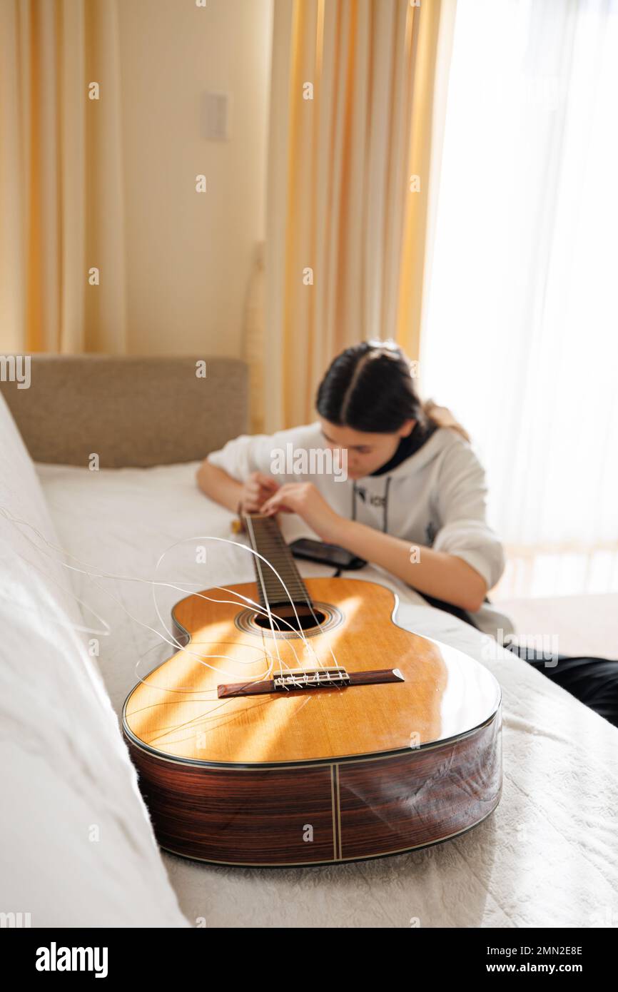 Teenage girl with long brown hair and white hoody changing strings in ...