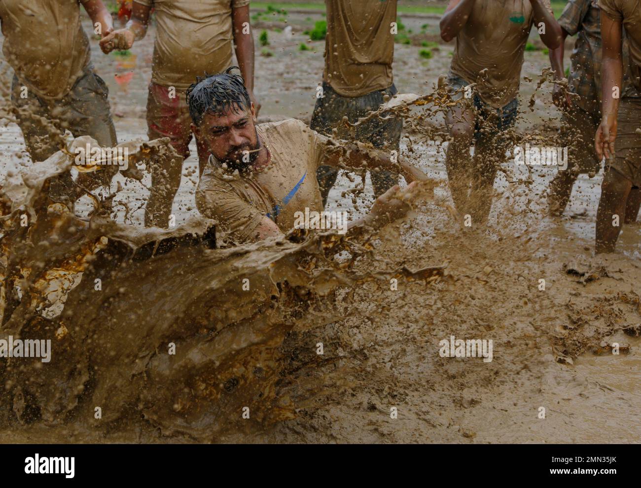 Nepalese men play in the mud in a paddy field during Asar Pandra, or ...