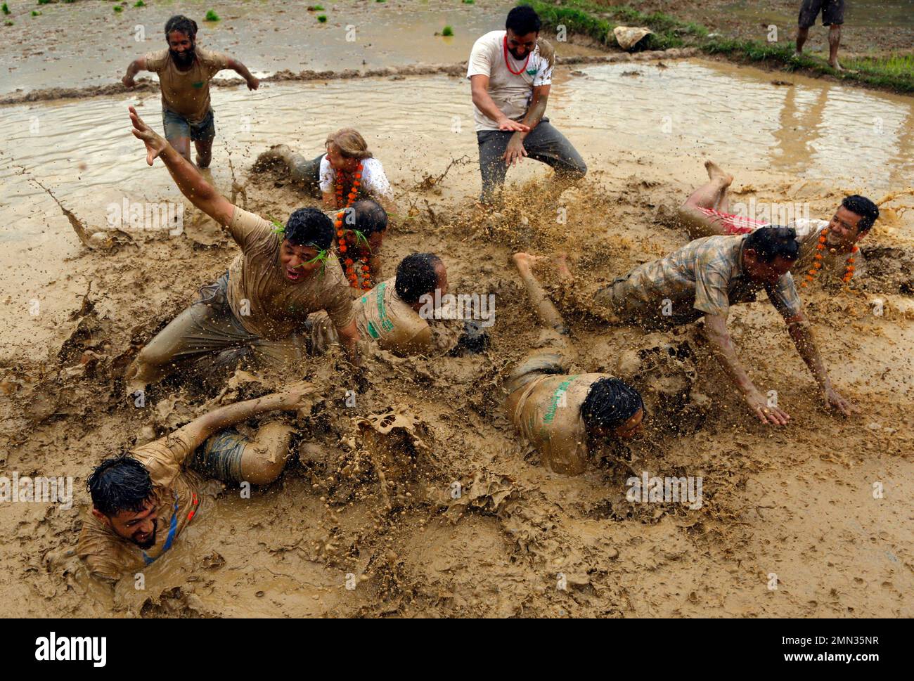 Nepalese men play in the mud in a paddy field during Asar Pandra, or ...