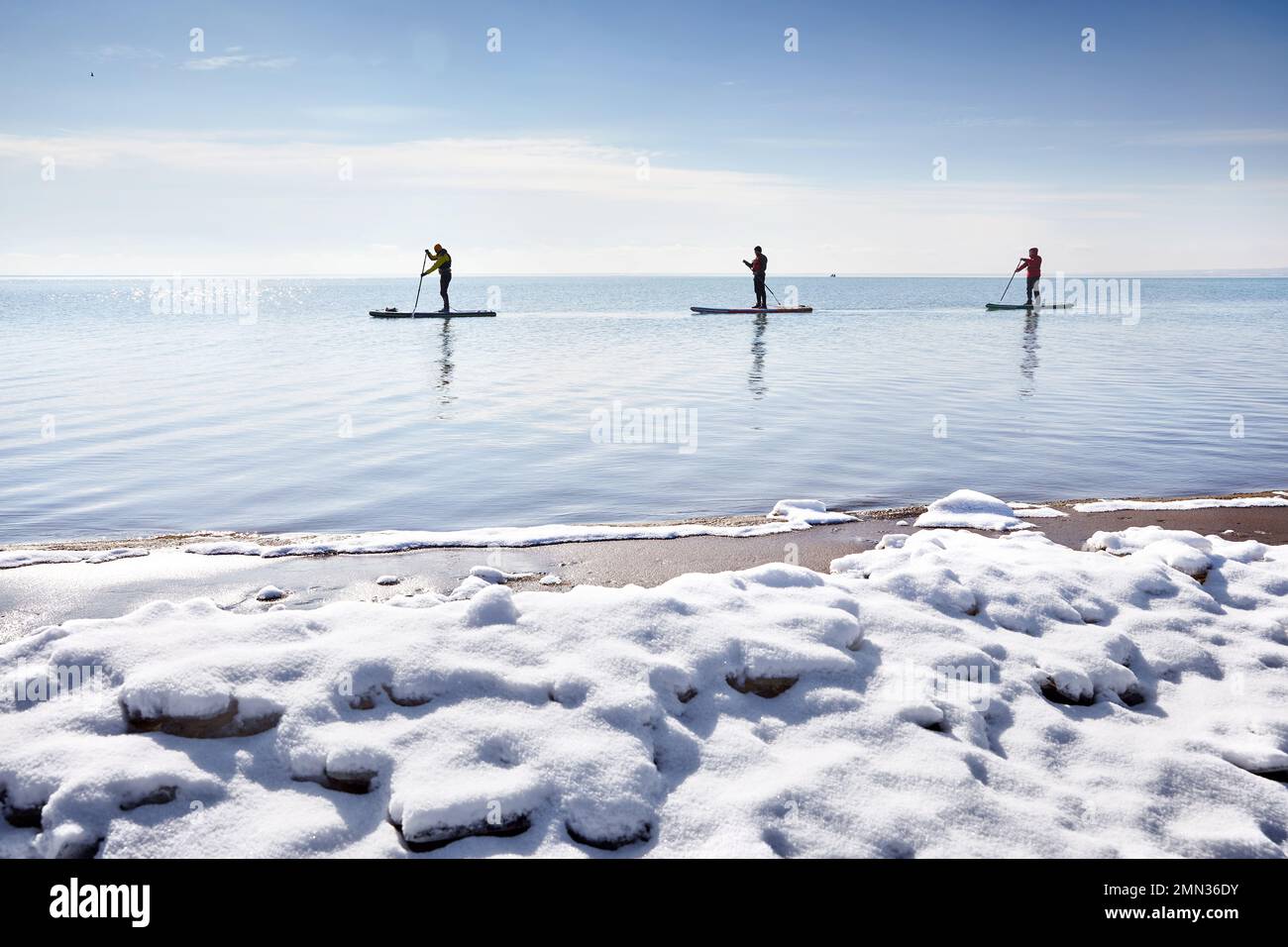 Three Man athlete is paddling on sup board in the lake with ice at ...