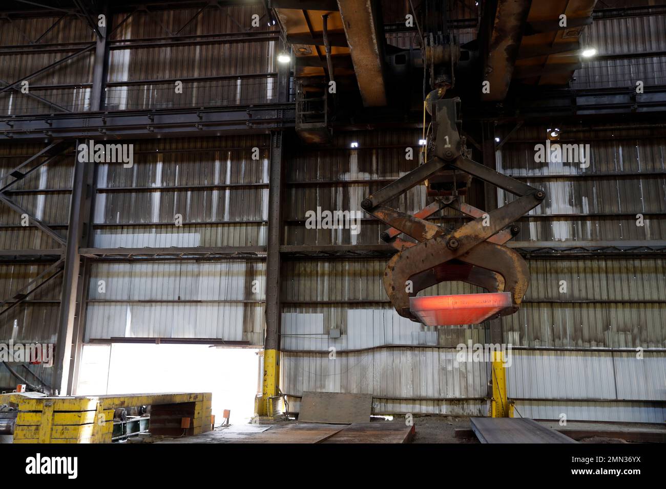 A newly formed slab of steel glows red as it is hoisted into the air to ...