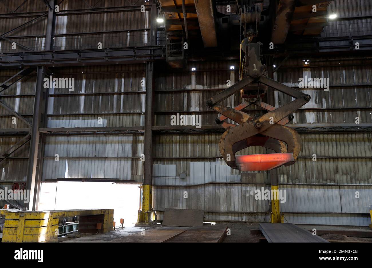 A newly formed slab of steel glows red as it is hoisted into the air to ...