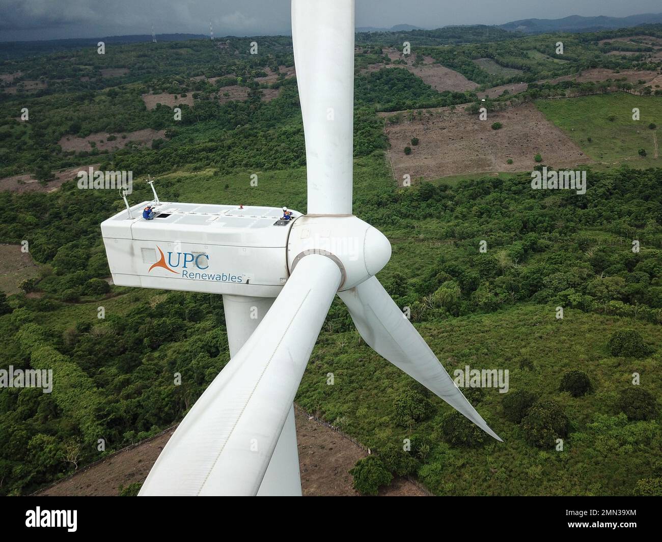 Two wind turbine technicians work on the nacelle of a turbine in the ...