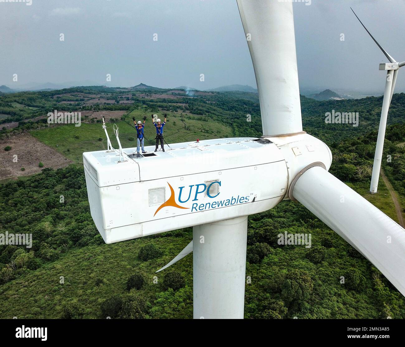 Two wind turbine technicians work on the nacelle of a turbine in the ...