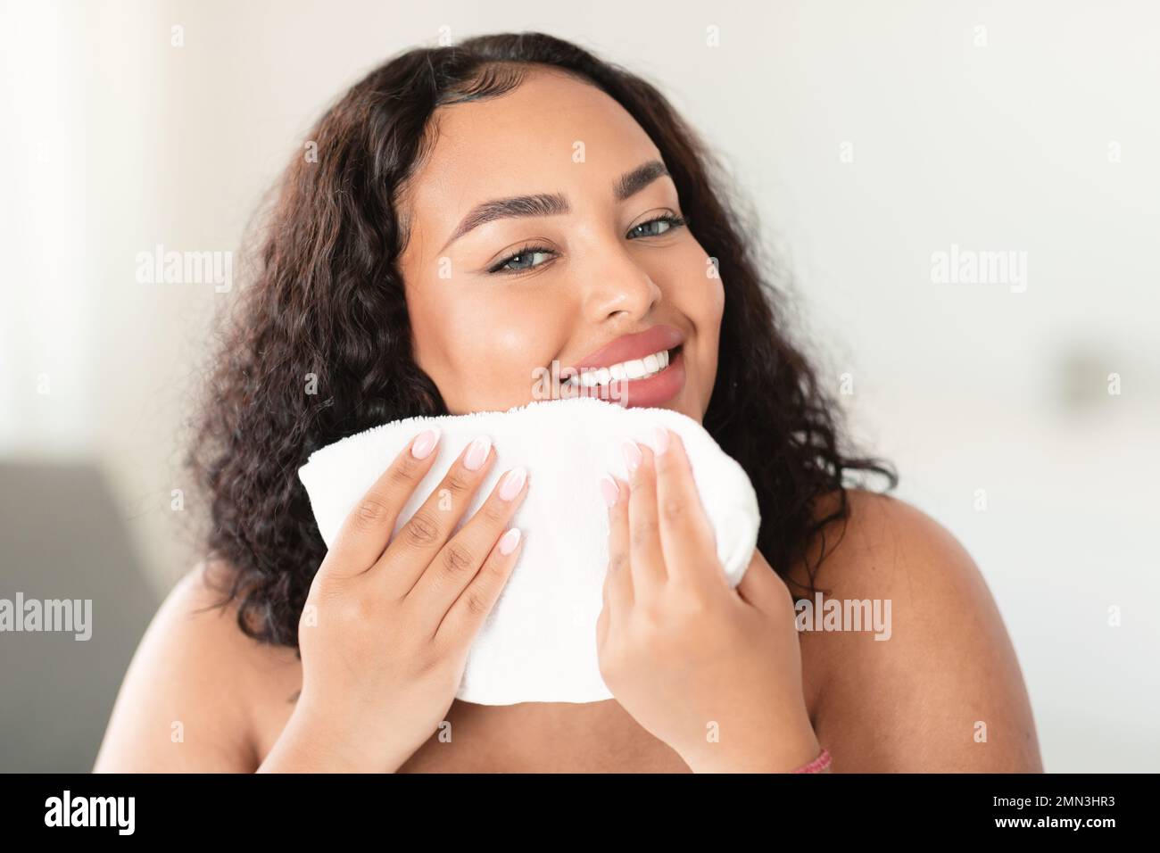 Facial skincare and hygiene concept. Plus size lady drying face with ...