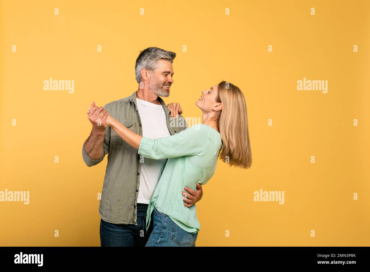 Loving middle aged spouses dancing and having fun over yellow studio ...