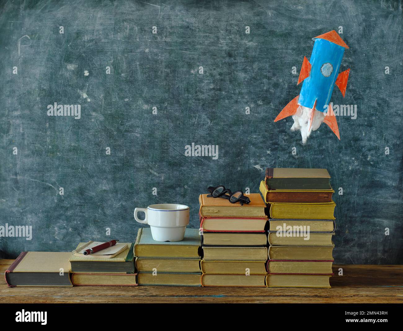 Stack of hardback books with rocket launching on blackboard background ...