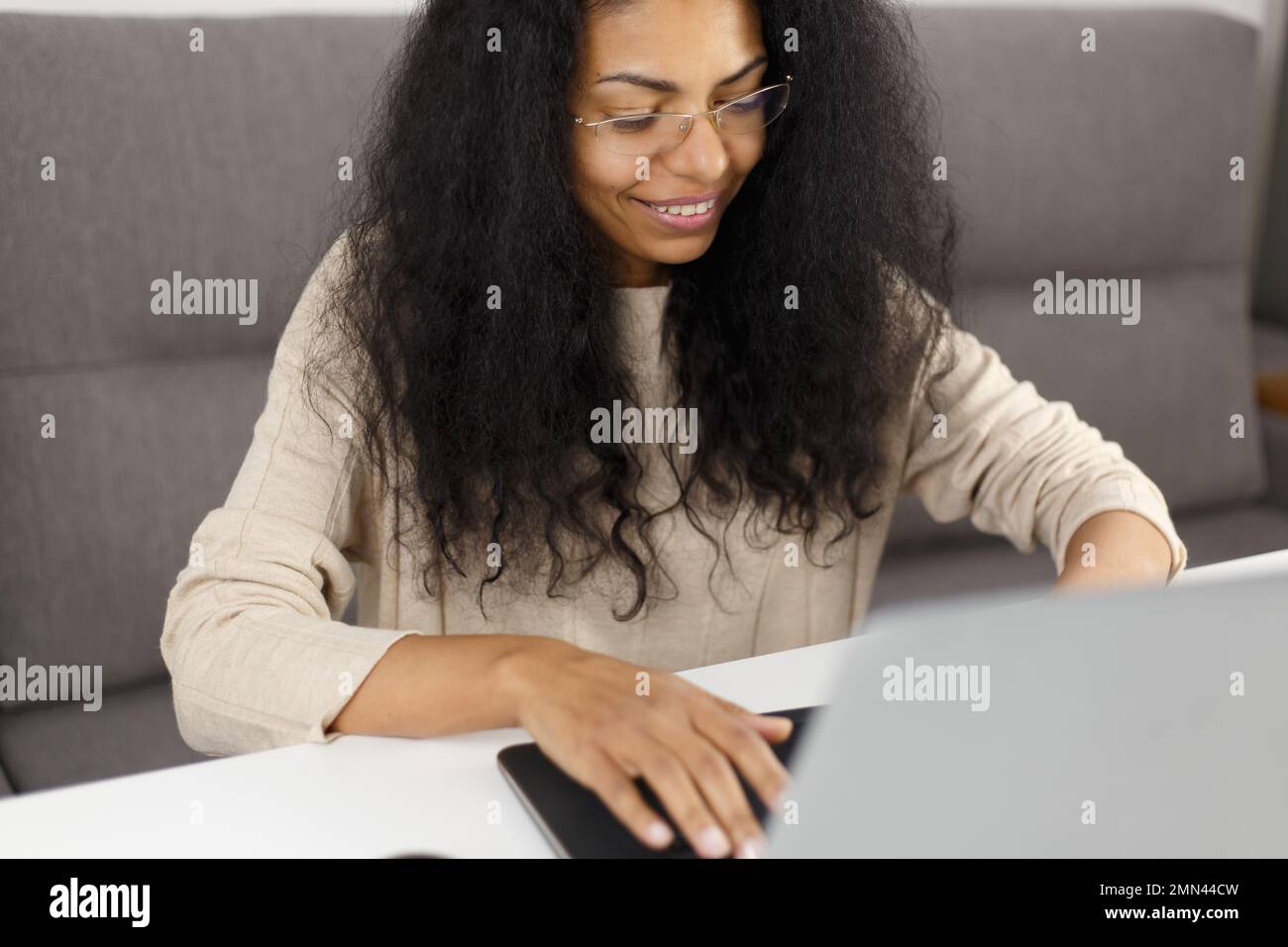 Cheerful BIPOC woman works on laptop computer at home. Friendly POC female typing text on ...