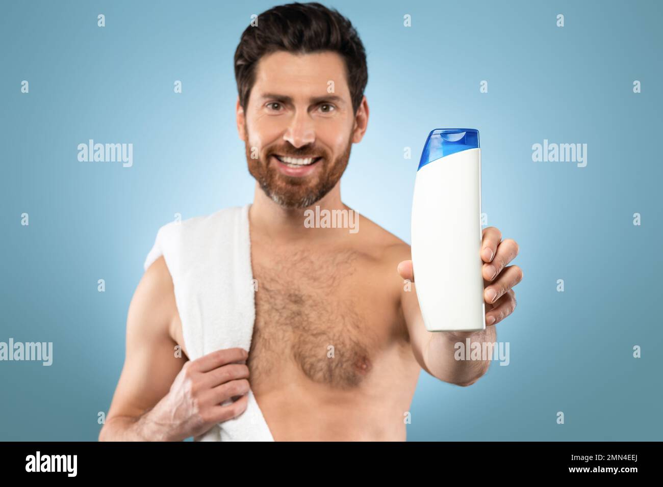 Happy handsome man showing shampoo bottle, standing with towel over ...