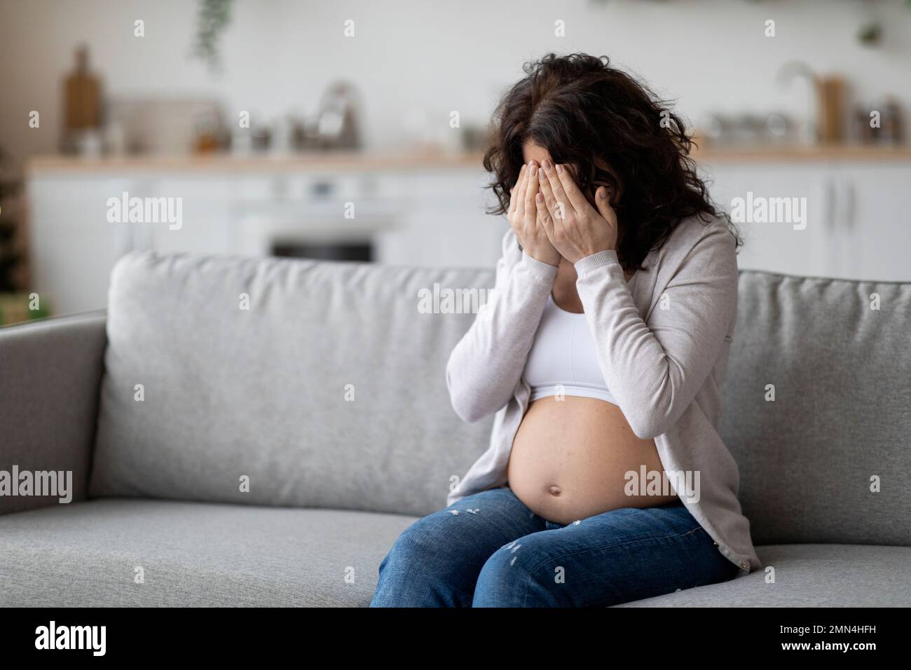 Portrait Of Young Pregnant Woman Crying While Sitting On Couch At Home ...