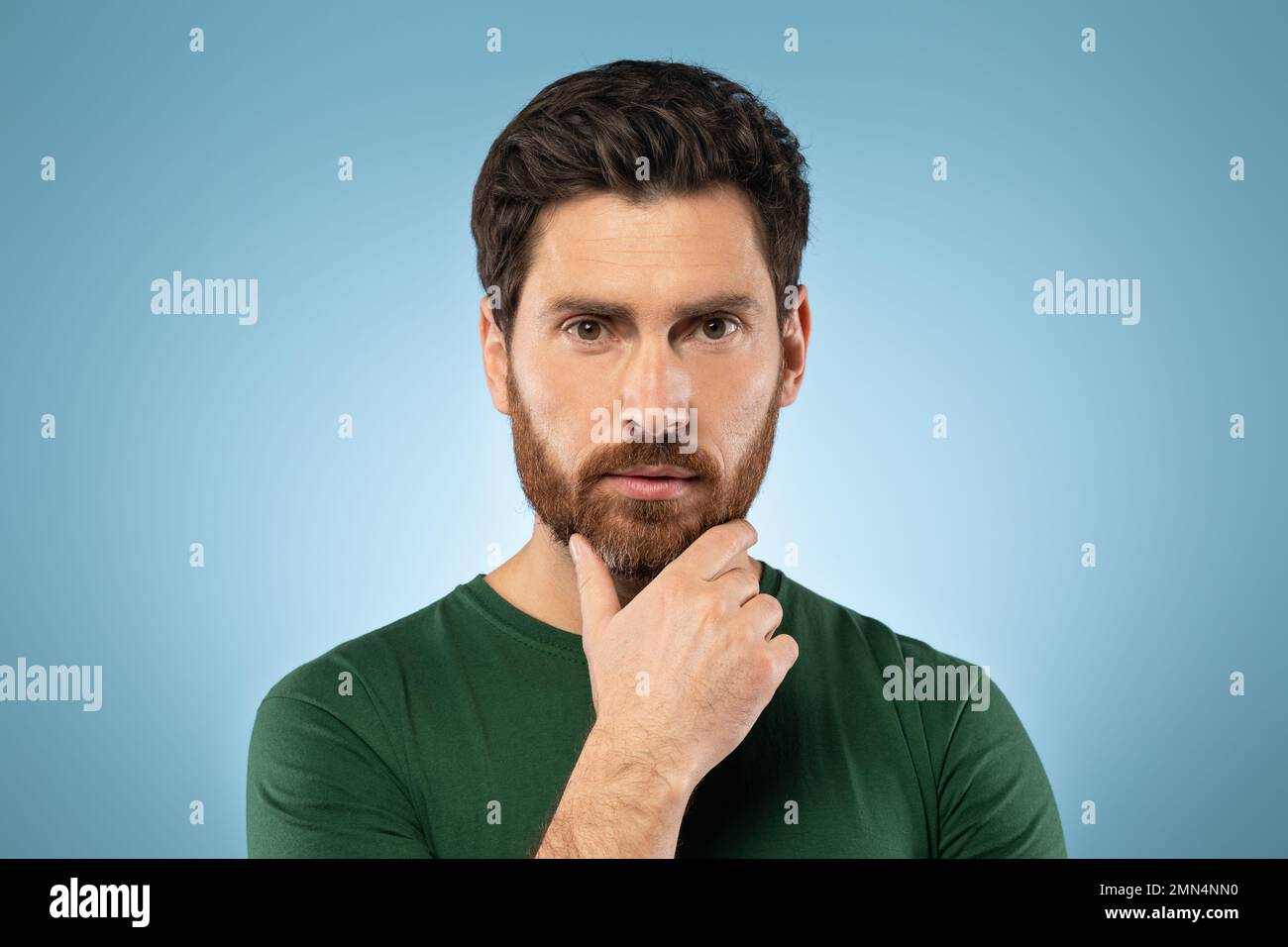 Portrait of handsome bearded caucasian man posing over blue background and touching chin Stock ...