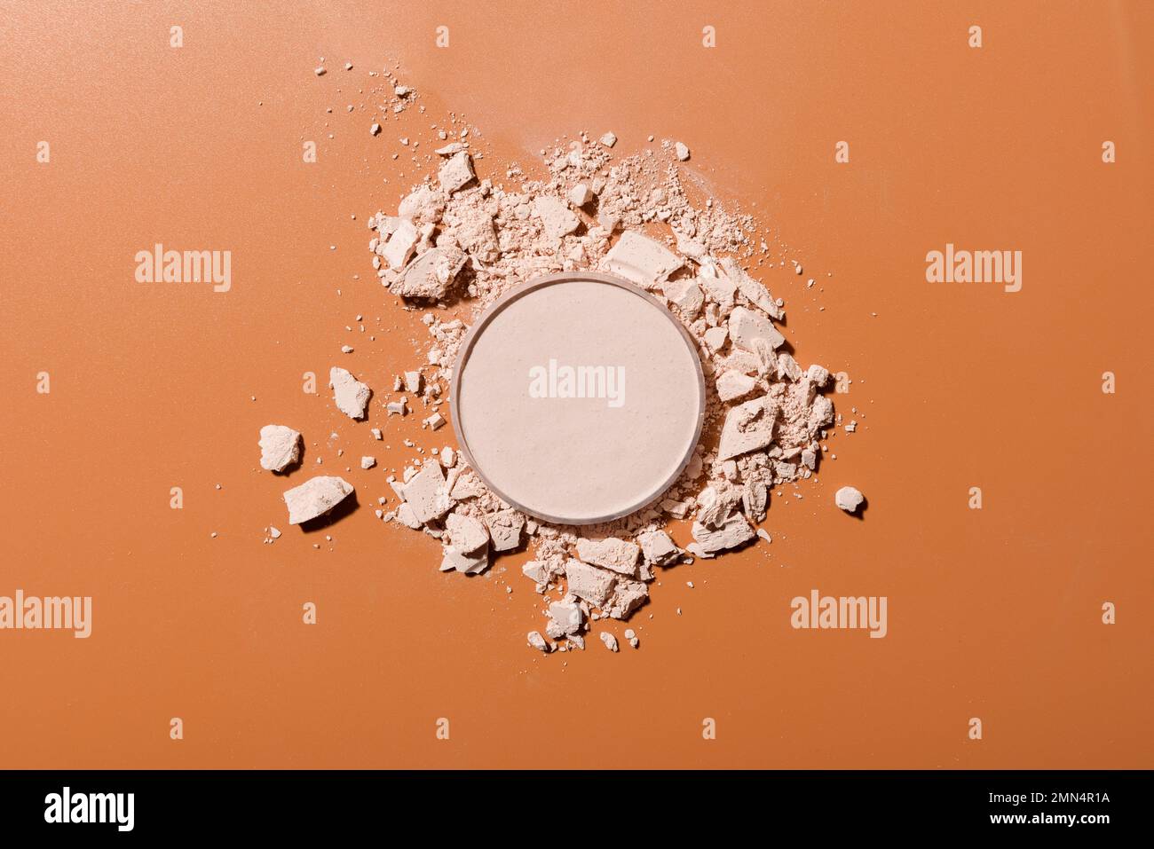 Crushed face powder heap and round box of pressed one on top on brown ...