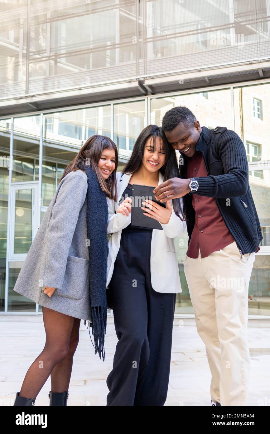 Attractive coworkers using a tablet outside the office. Group of young ...