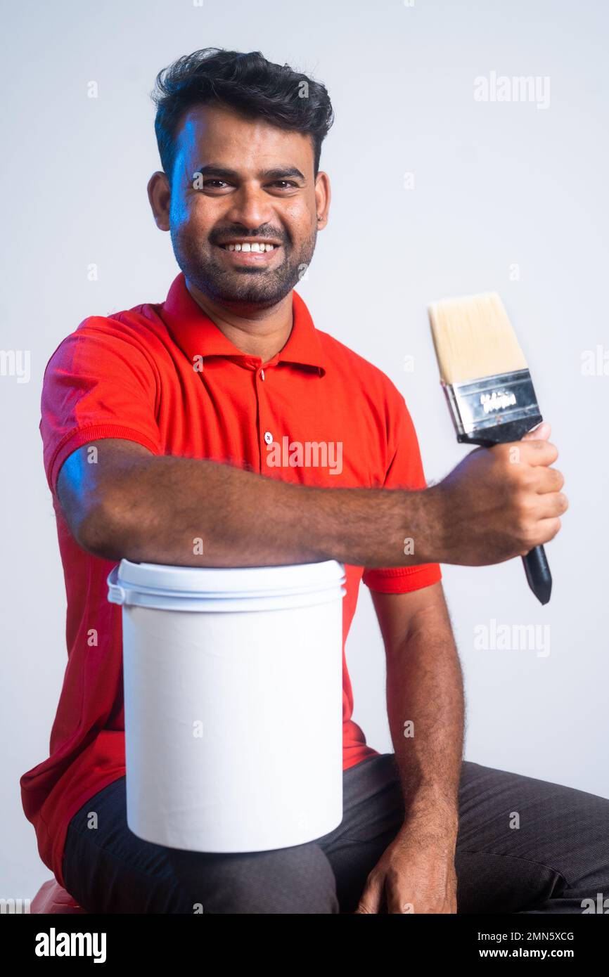 Vertical shot of smiling painter holding paint brush and bucket by ...