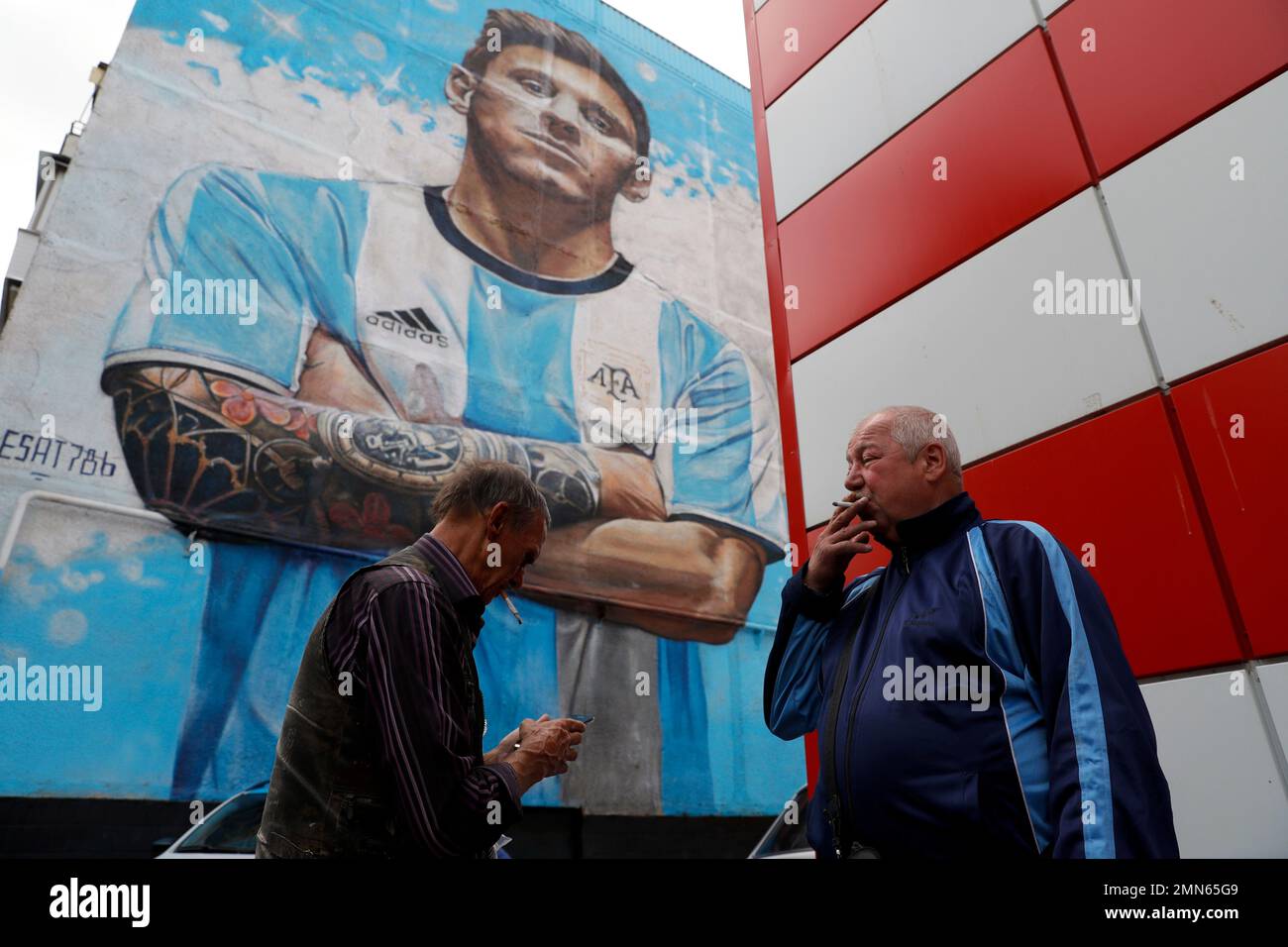 Men share a smoke under a mural of Argentina's soccer star Lionel Messi ...