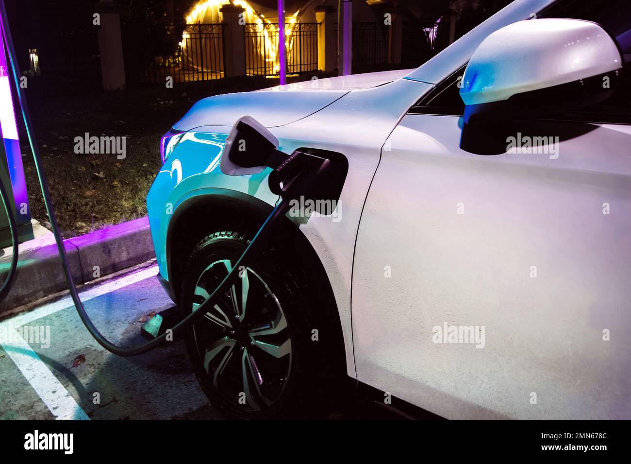 The white car is connected to the electric charging station at night in ...