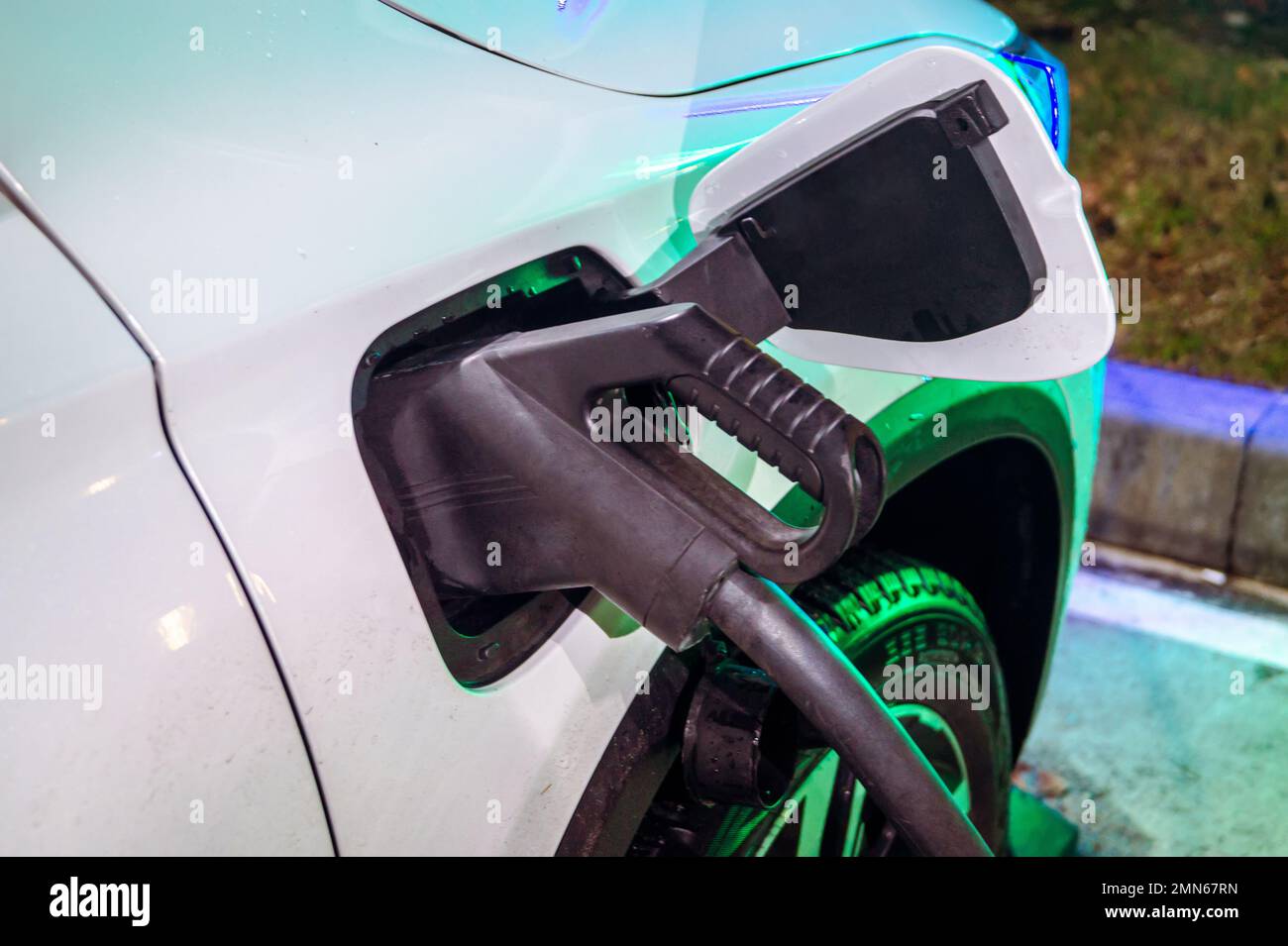 The white car is connected to the electric charging station at night in ...