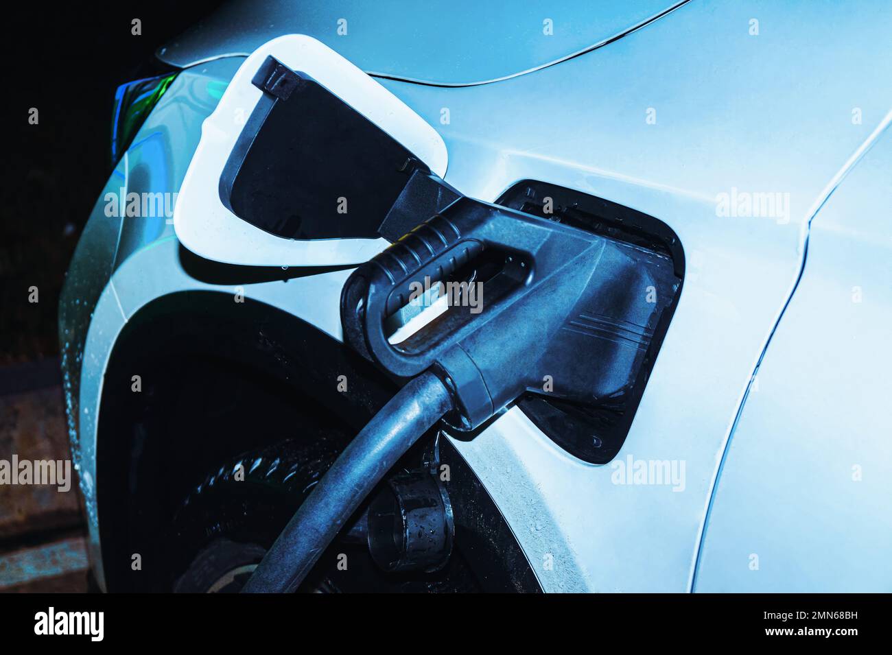 The white car is connected to the electric charging station at night in ...