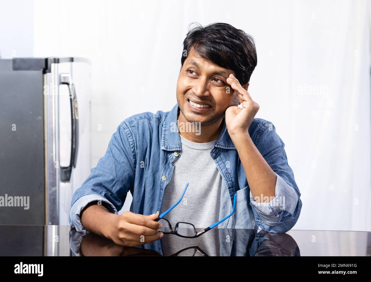 An Indian male with spectacles facing headache sitting beside a table ...