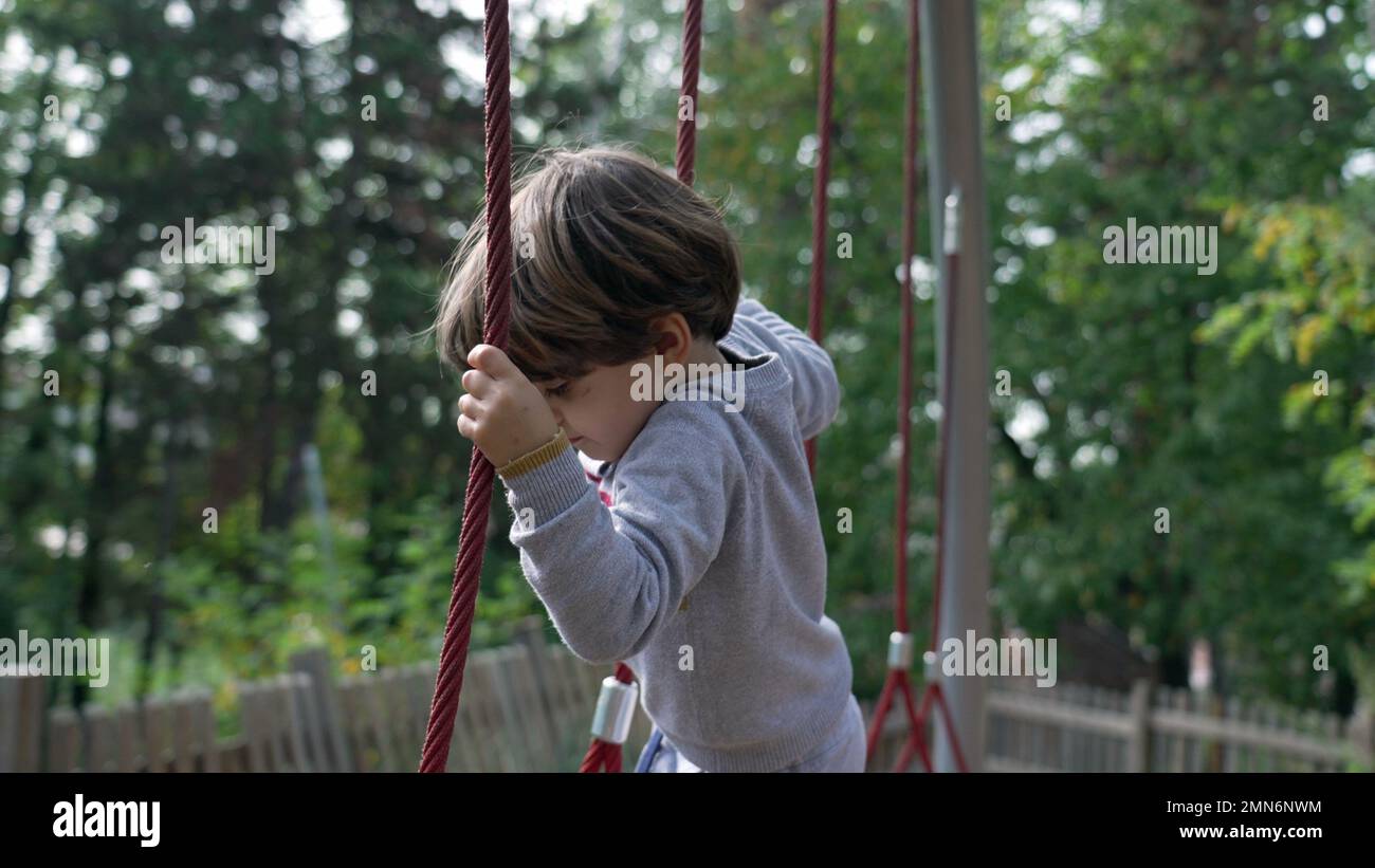 Active child keeping balance at playground structure with ropes. One ...
