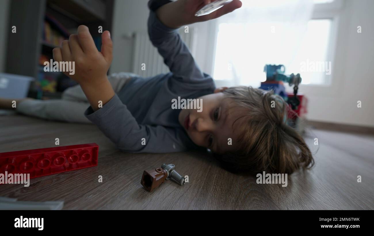 One small boy laying on bedroom floor playing by himself. Little boy at ...