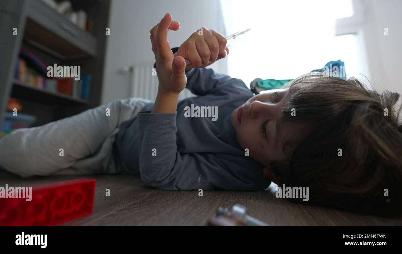 One small boy laying on bedroom floor playing by himself. Little boy at ...
