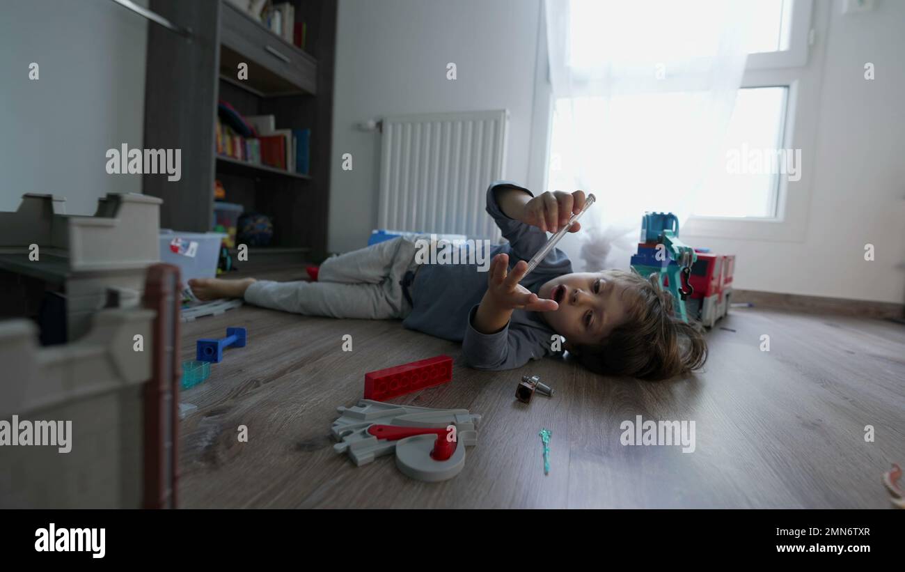 One small boy laying on bedroom floor playing by himself. Little boy at ...