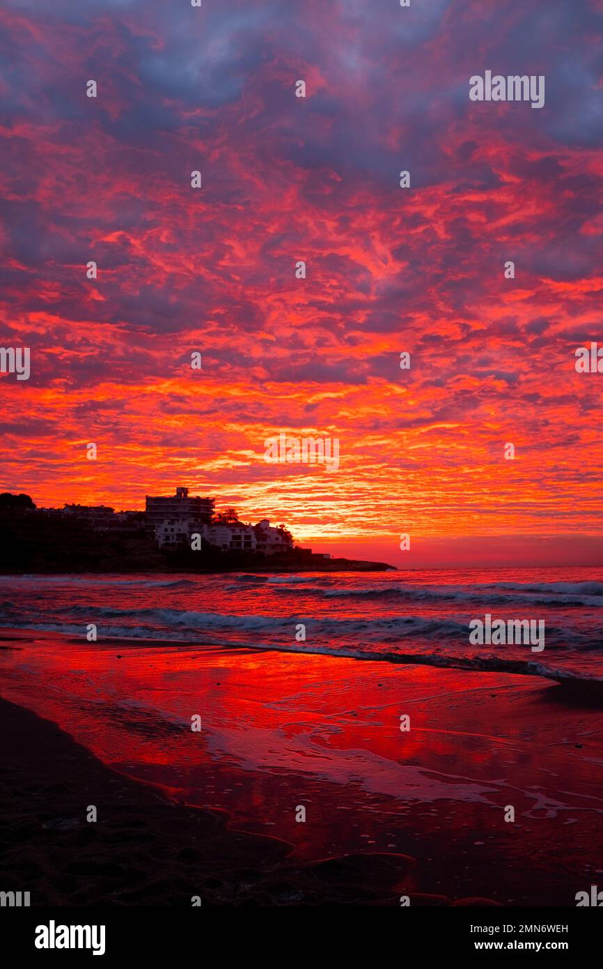 Red sunset at the beach with town in silhouette and dramatic sky with ...