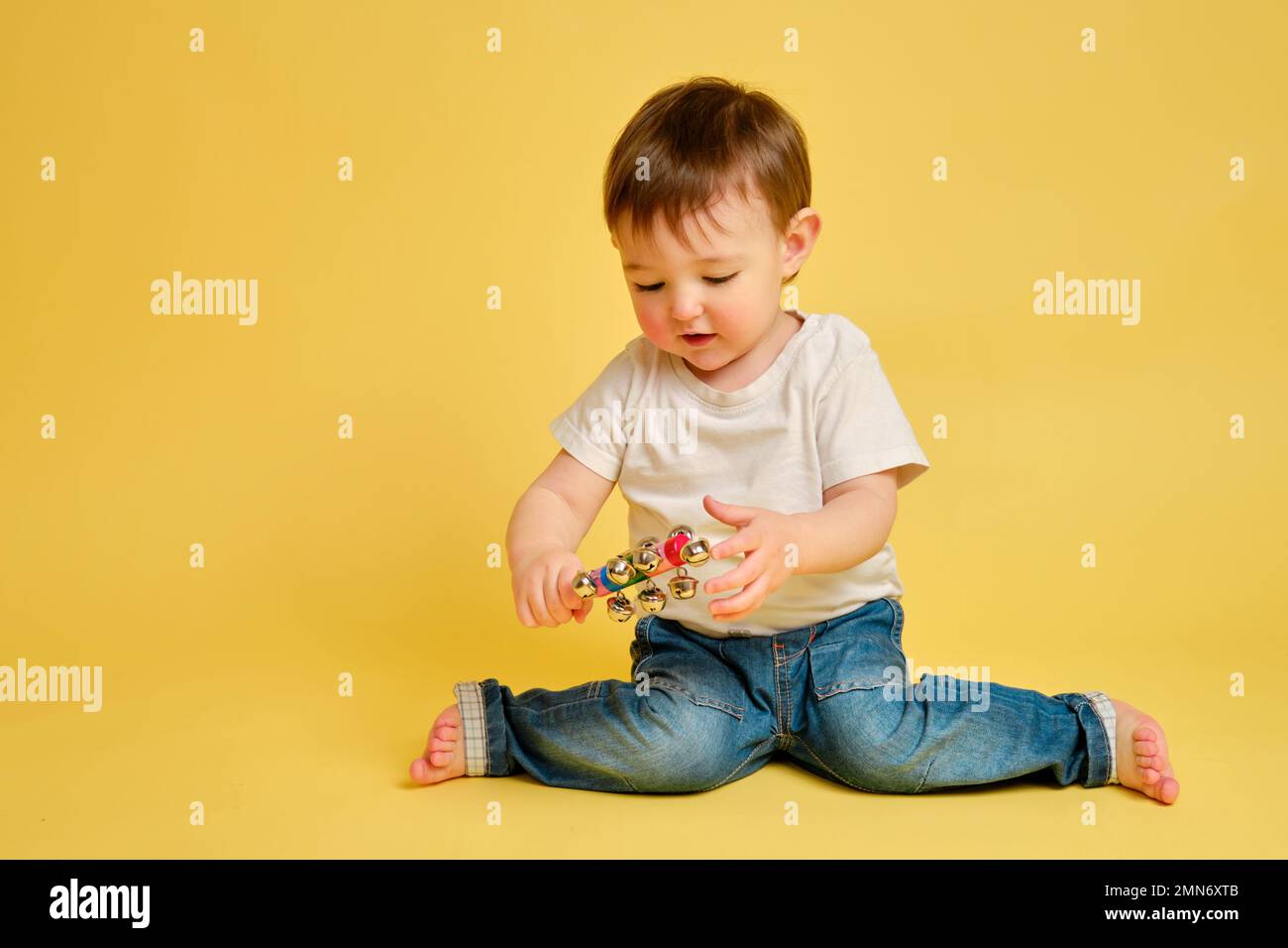 Toddler baby plays with a musical rattle bells on a stick, studio ...