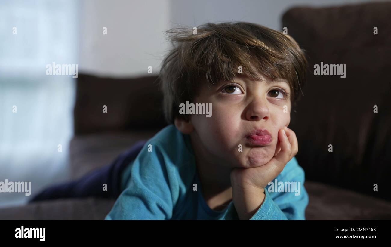 Little boy laying on couch with pensive expression and hand in chin ...