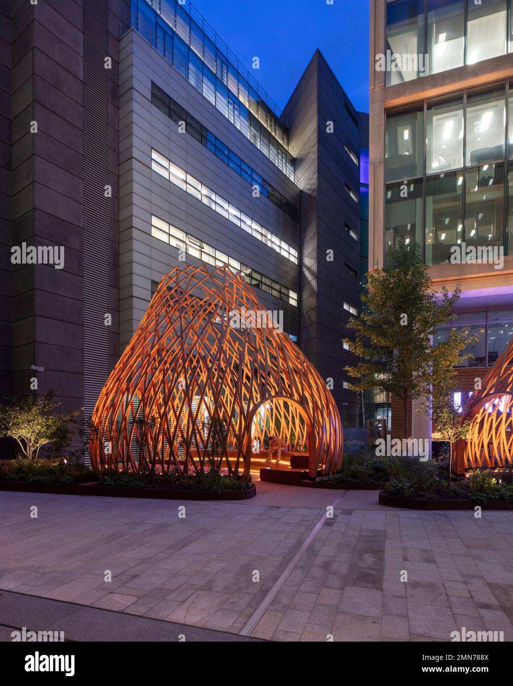 Wooden pavilion illuminated and glowing up against an office building ...