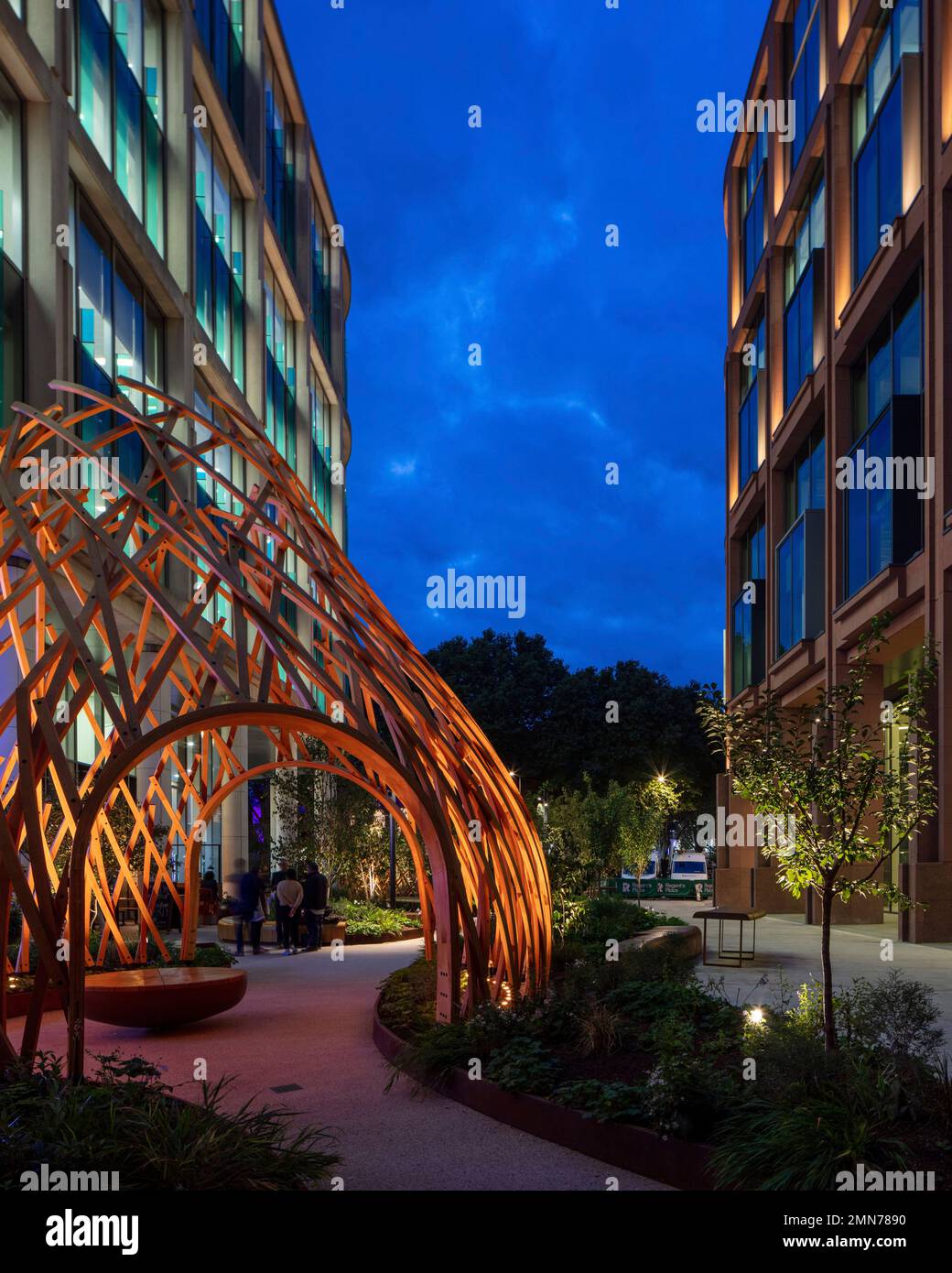 Wooden pavilion illuminated and glowing up against an office building ...