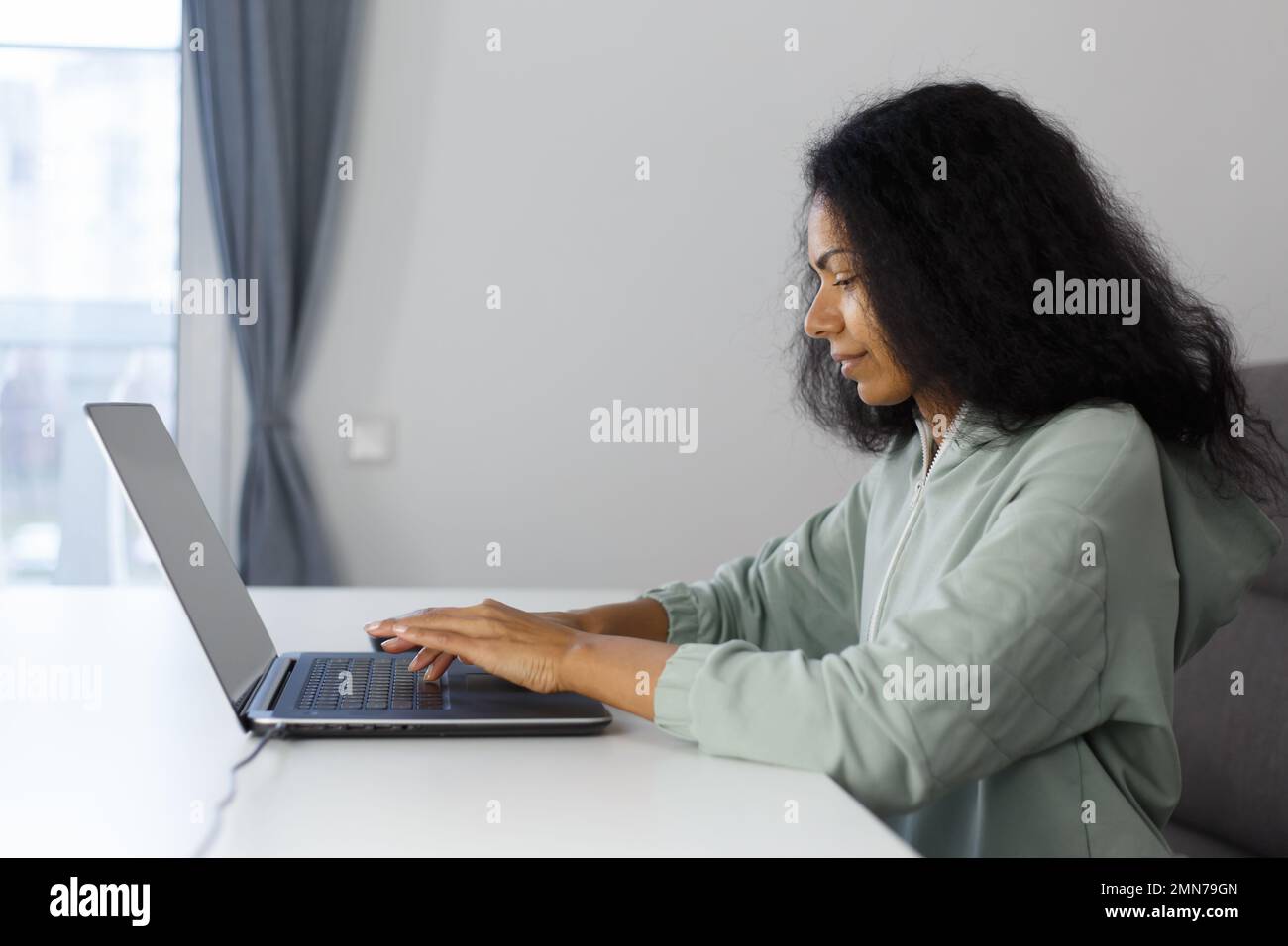Focused BIPOC woman typing text on notebook keyboard. Programmer coding on laptop computer at ...