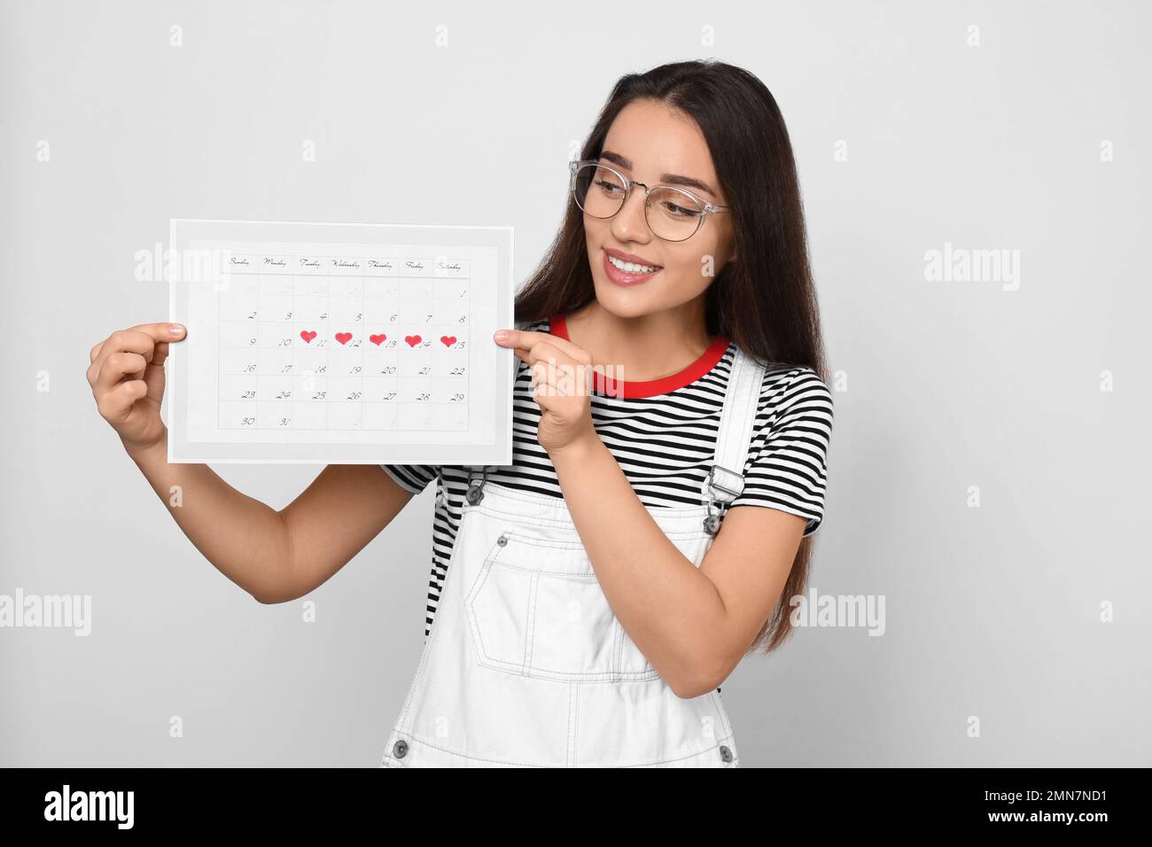 Young woman holding calendar with marked menstrual cycle days on light ...
