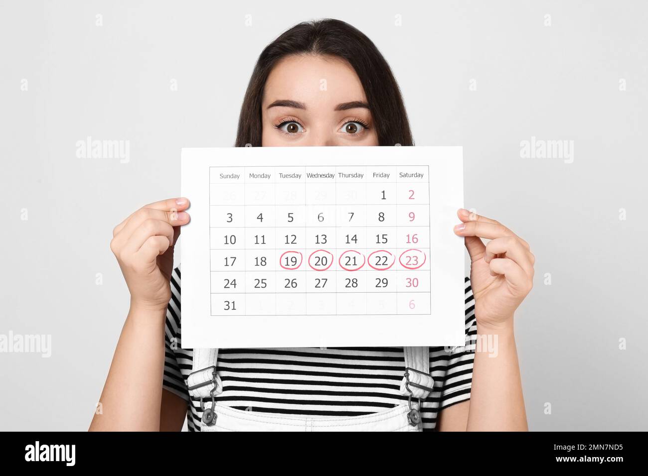 Young woman holding calendar with marked menstrual cycle days on light ...