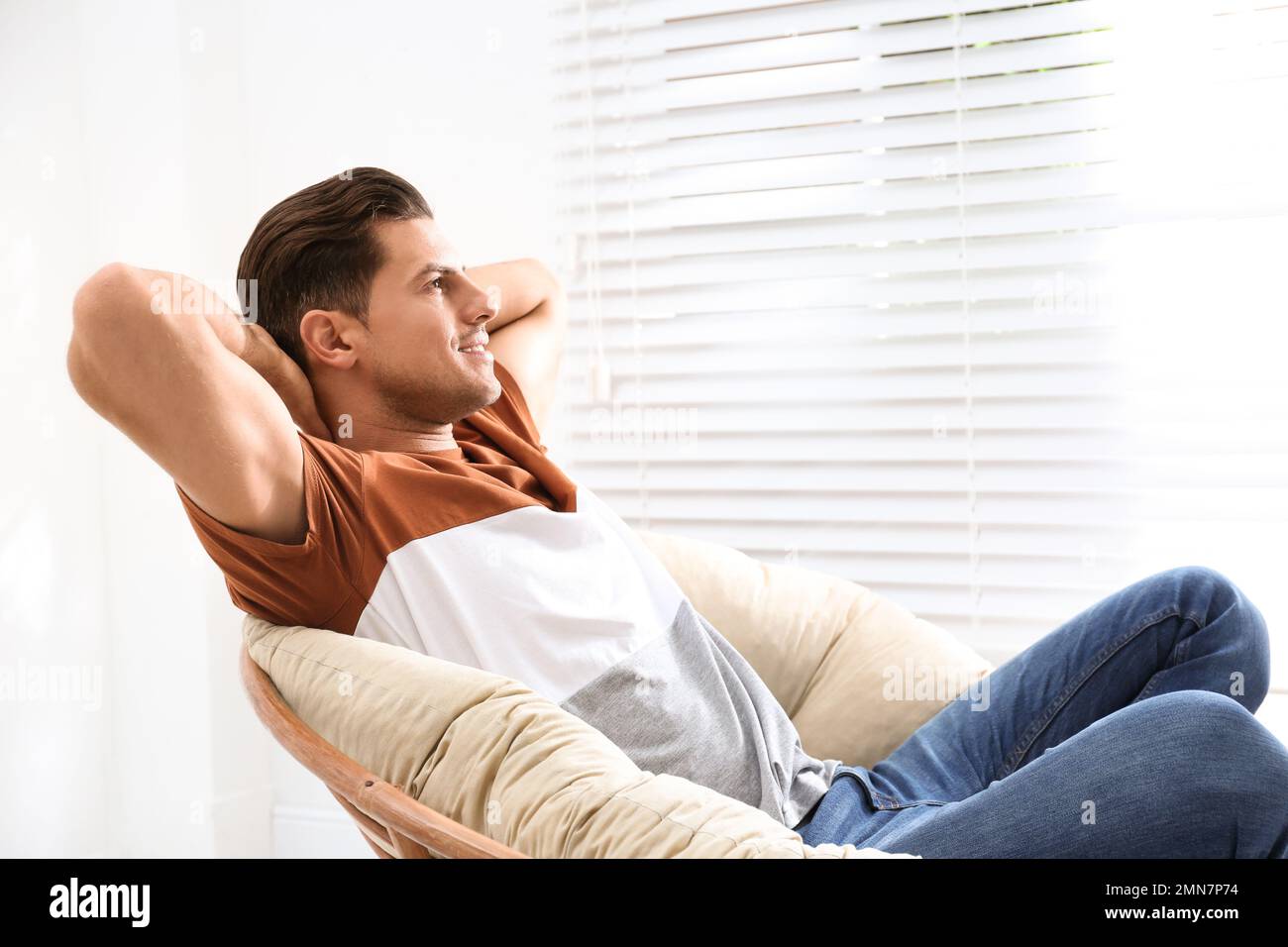 Attractive man relaxing in papasan chair near window at home Stock ...