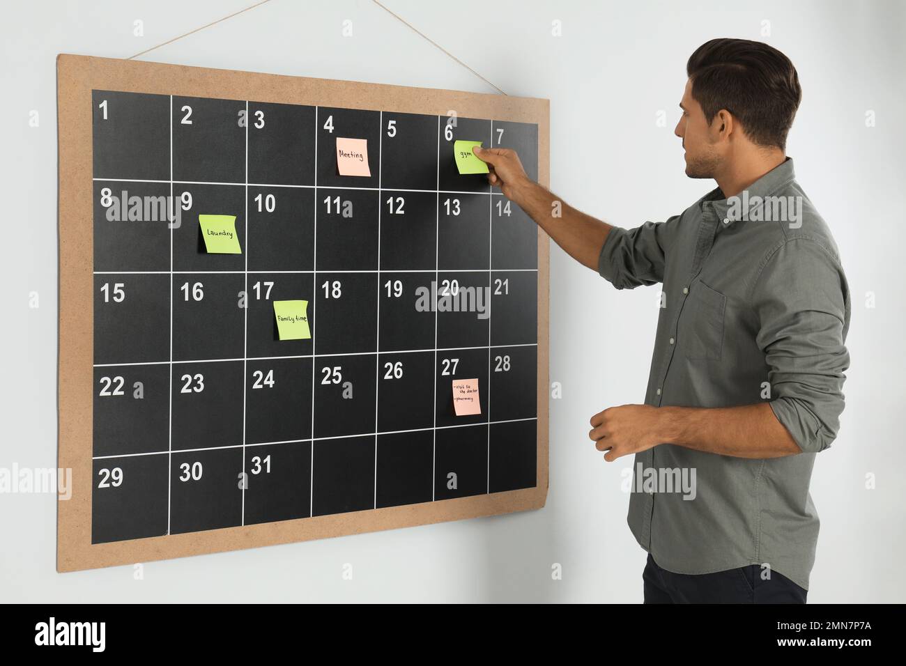 Handsome man putting sticky note on board calendar Stock Photo - Alamy
