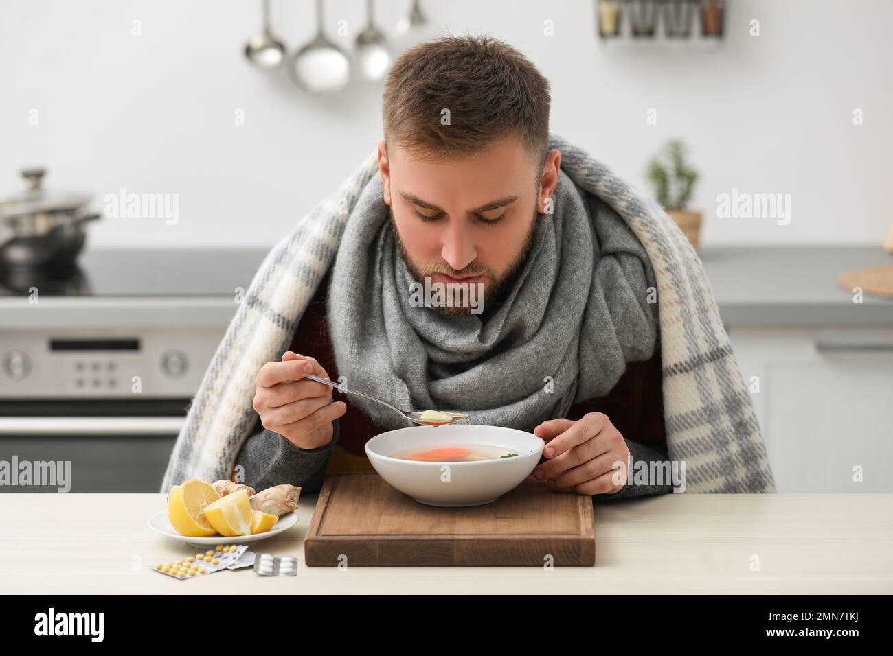 Sick young man eating tasty soup to cure flu at table in kitchen Stock ...