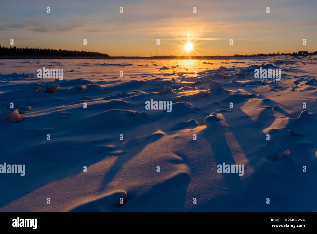 The bright winter sun sets over the forest on the horizon, casting ...