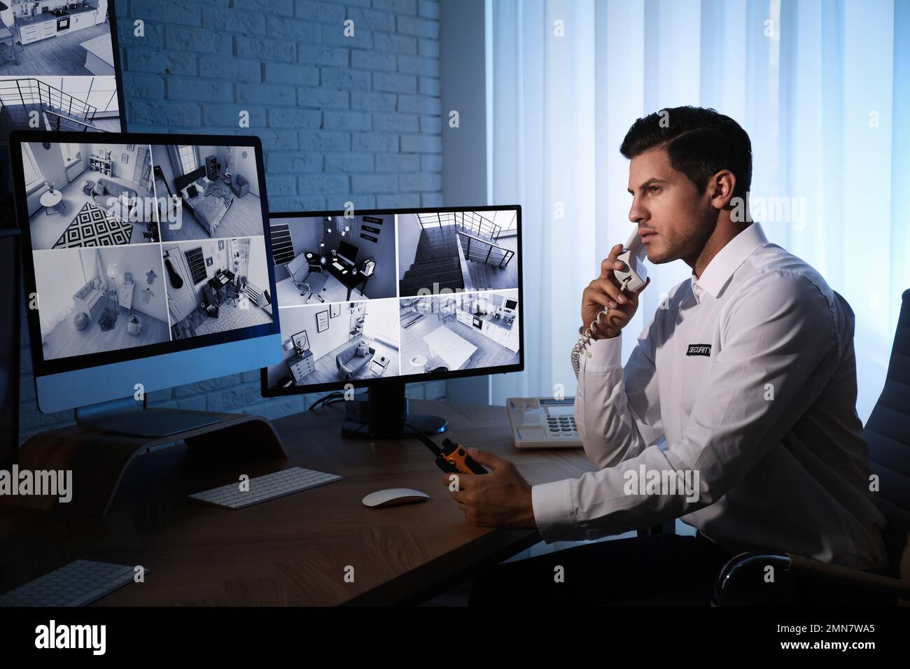 Male security guard talking by telephone near monitors at workplace ...