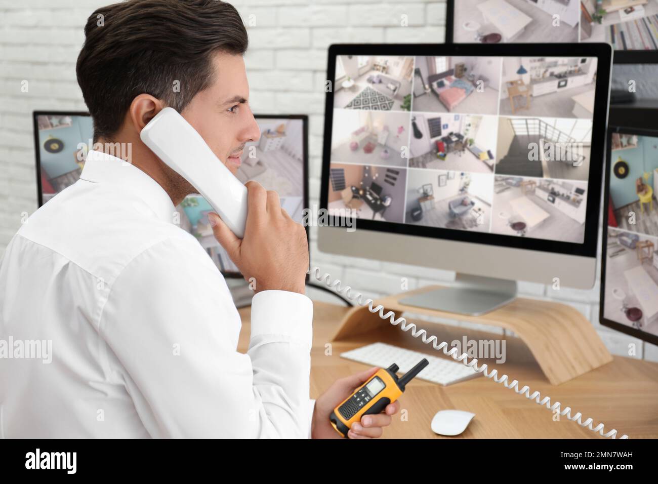 Male security guard talking by telephone near monitors at workplace ...